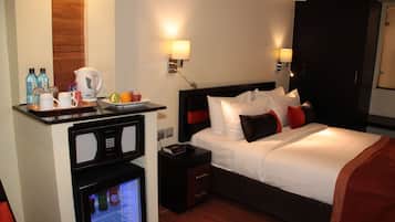 Quarto de hotel com cama, mesas de cabeceira, minibar e televisão na parede.