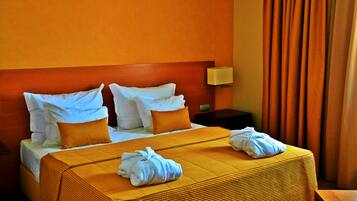 Quarto de hotel com uma cama grande, duas almofadas, uma mesa de cabeceira com abajur e uma janela com cortinas.