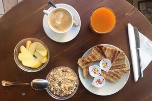 Mesa de madeira com café, sumo de laranja, torradas, iogurte e granola para o pequeno-almoço.