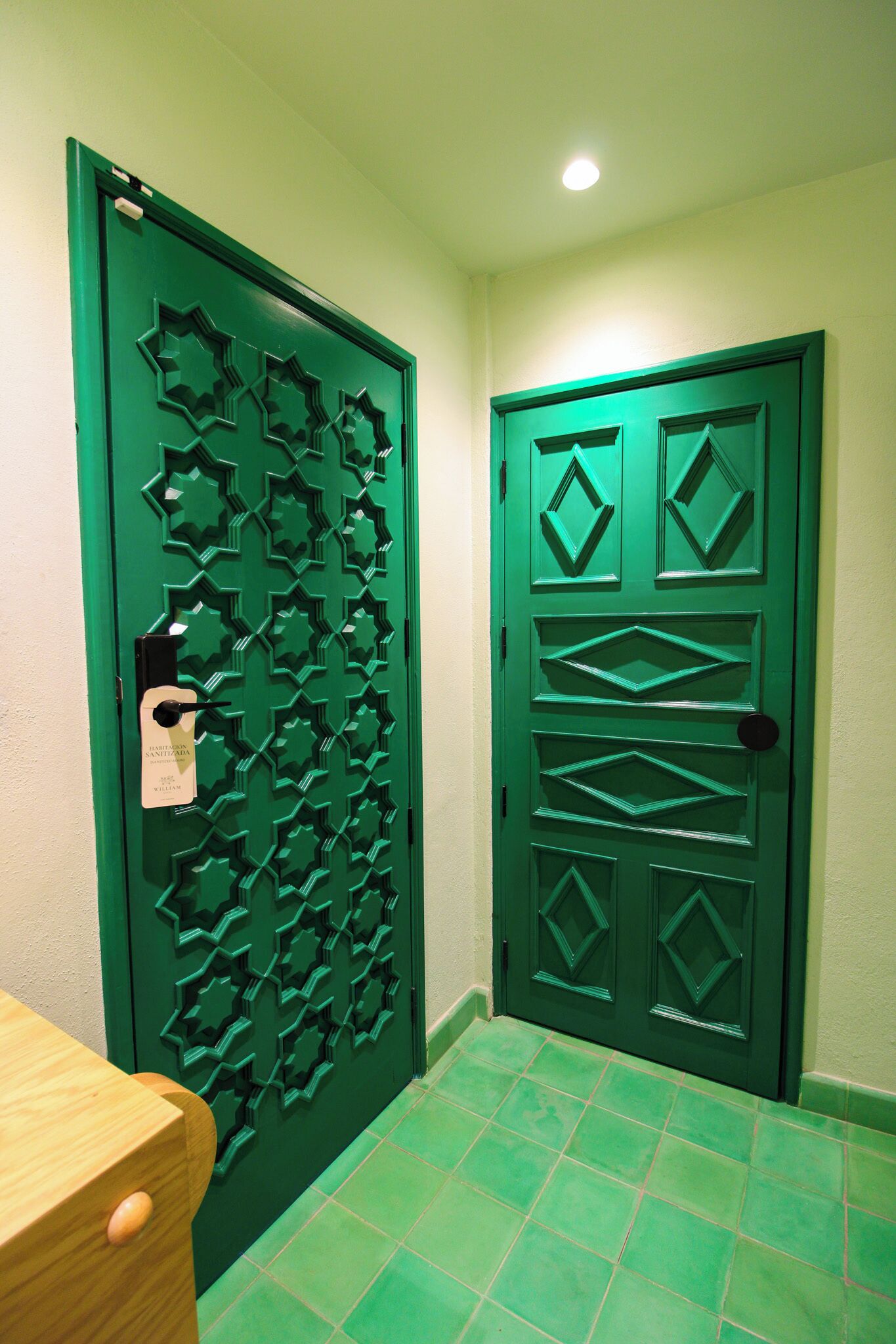 Uma porta verde com padrões de estrelas e diamantes, um banco de madeira e piso de azulejos verdes.