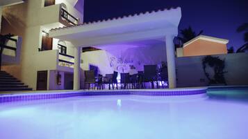 Uma área da piscina com um espaço de estar coberto, uma placa indicando "Poolside Cafe" e uma escadaria para um andar superior.