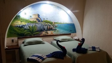 Quarto com duas camas, um mural com paisagem costeira e uma pequena estátua na cama.