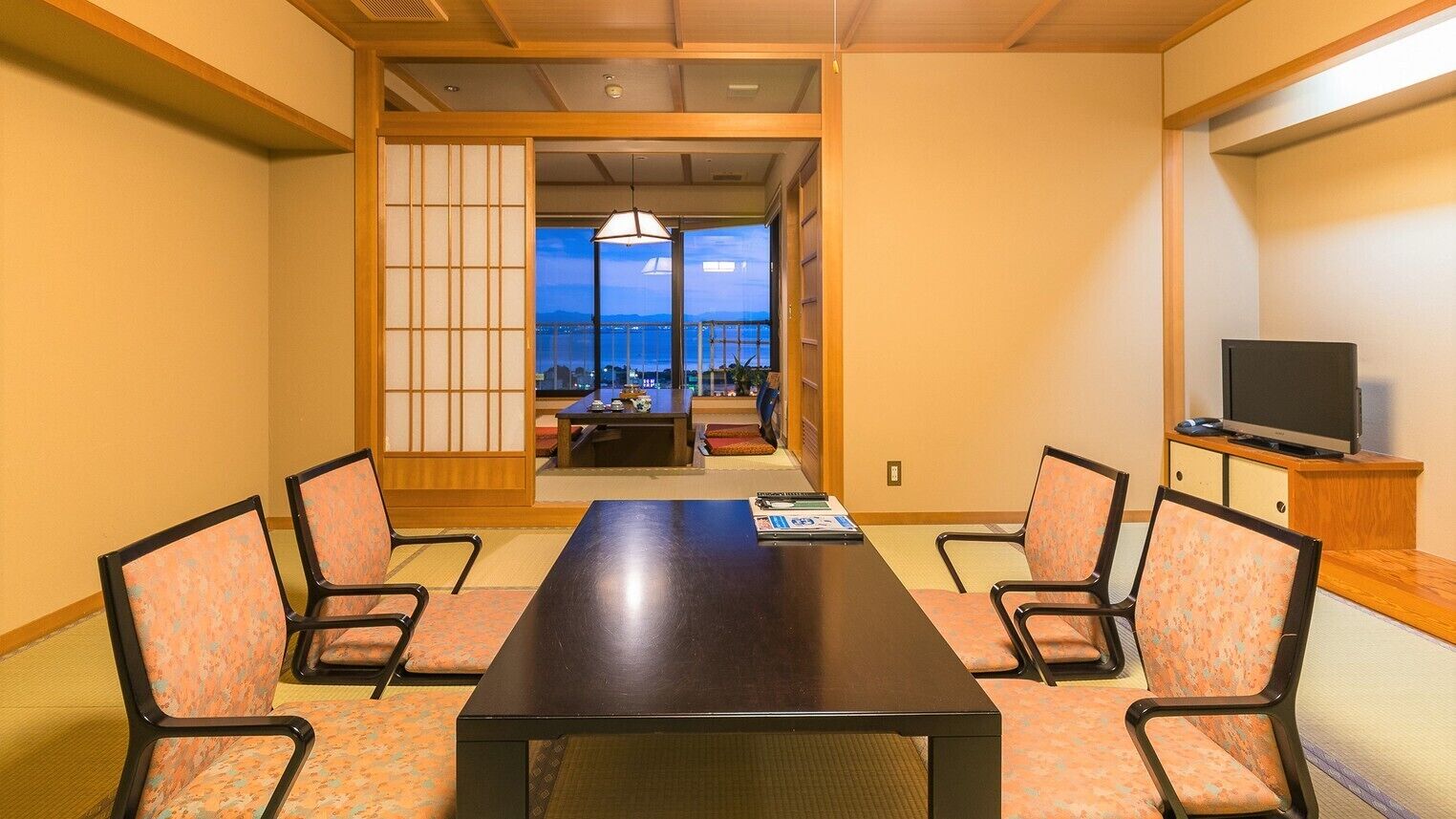 Quarto de hotel com mesa de jantar, quatro cadeiras, televisão e vista para a cidade.