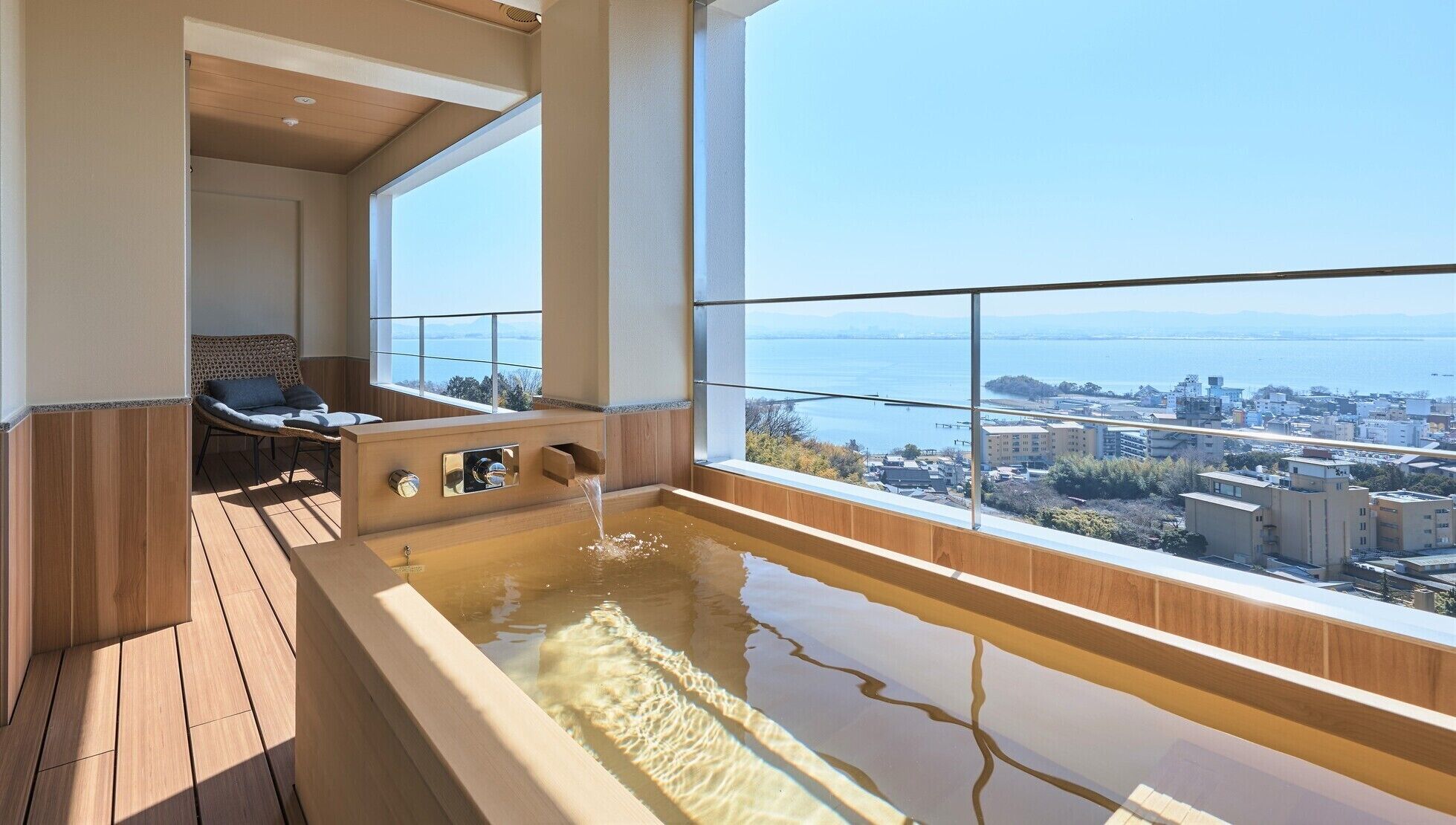 Uma casa de banho moderna com uma banheira grande, soalho de madeira e vista para a cidade e para a água.