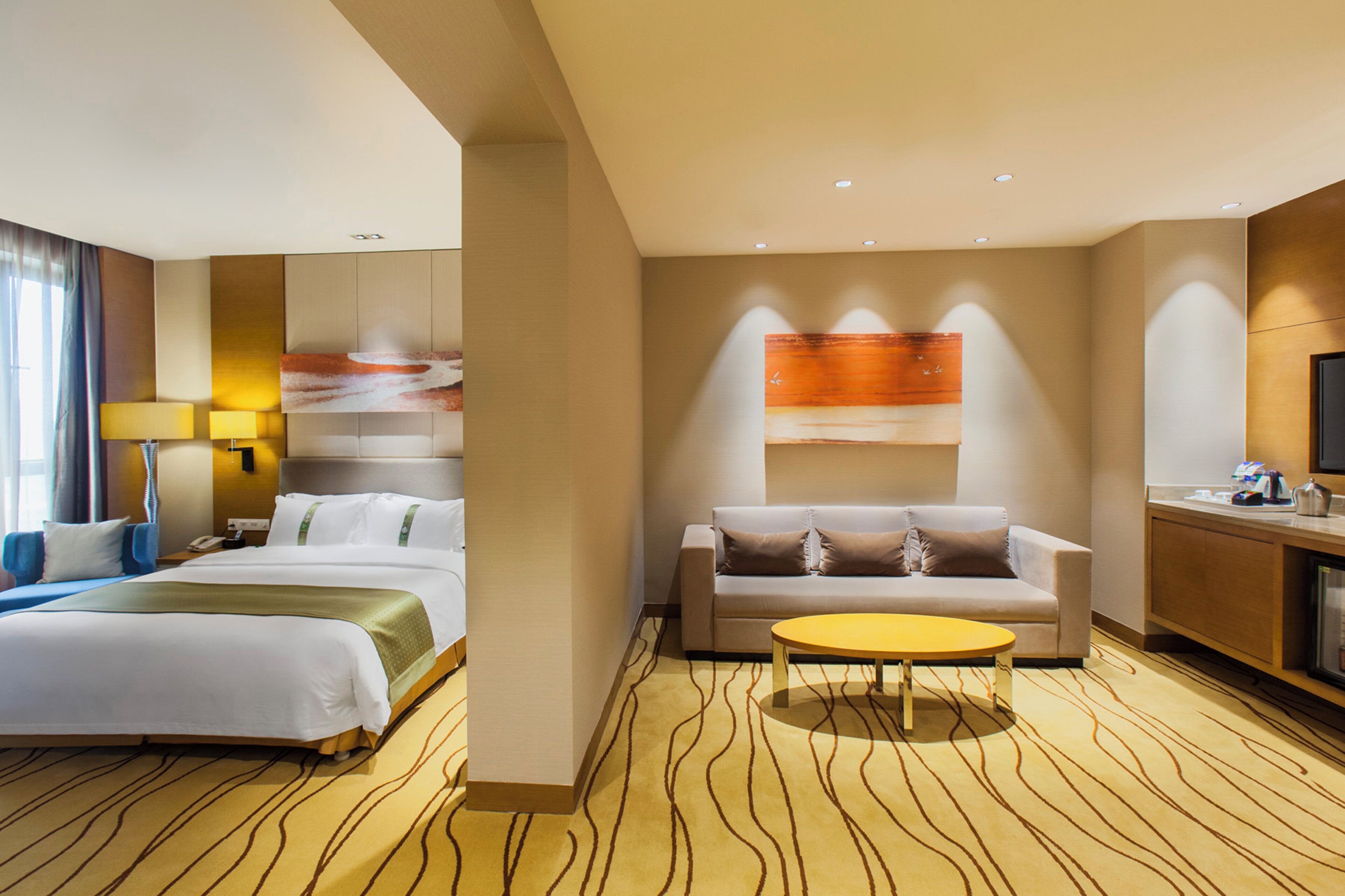 Quarto de hotel com cama, sofá, mesa de centro e televisão.