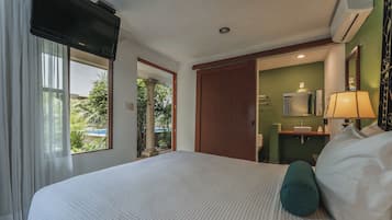 Quarto de hotel com uma cama grande, televisão, banheiro com espelho e vista para o verde lá fora.