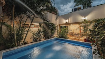 Piscina rodeada por vegetação exuberante e um edifício com área de estar ao ar livre.