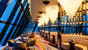 Um saguão de hotel moderno com uma ampla área de estar, carpete estampado e vista da cidade através de grandes janelas.