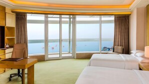Quarto de hotel com uma janela grande, uma escrivaninha, duas camas e uma cadeira.