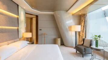 Quarto de hotel moderno com uma cama grande, um espaço de estar com uma mesinha e cadeiras, e uma janela ampla com vista.