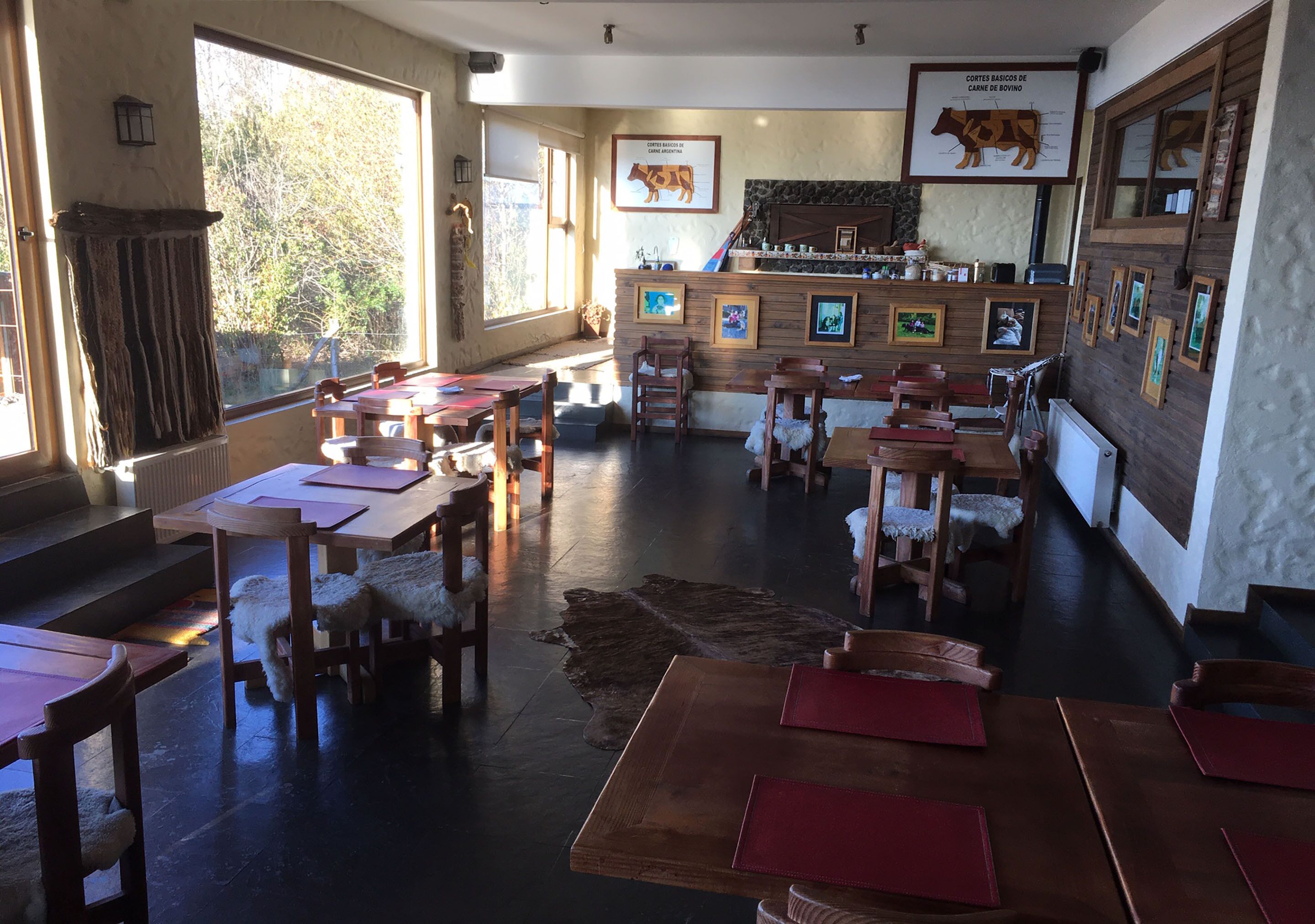 Um restaurante com mesas e cadeiras de madeira, um balcão com cardápio e quadros nas paredes.