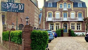 Um edifício histórico com uma placa indicando Hotel La Villa 10, apresentando fachada de tijolos, várias janelas e entrada com portão.