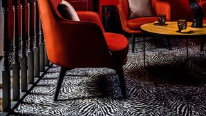 Quarto com paredes vermelhas, piso estampado com padrão de zebra, mesa redonda com cadeiras e luminária no teto.