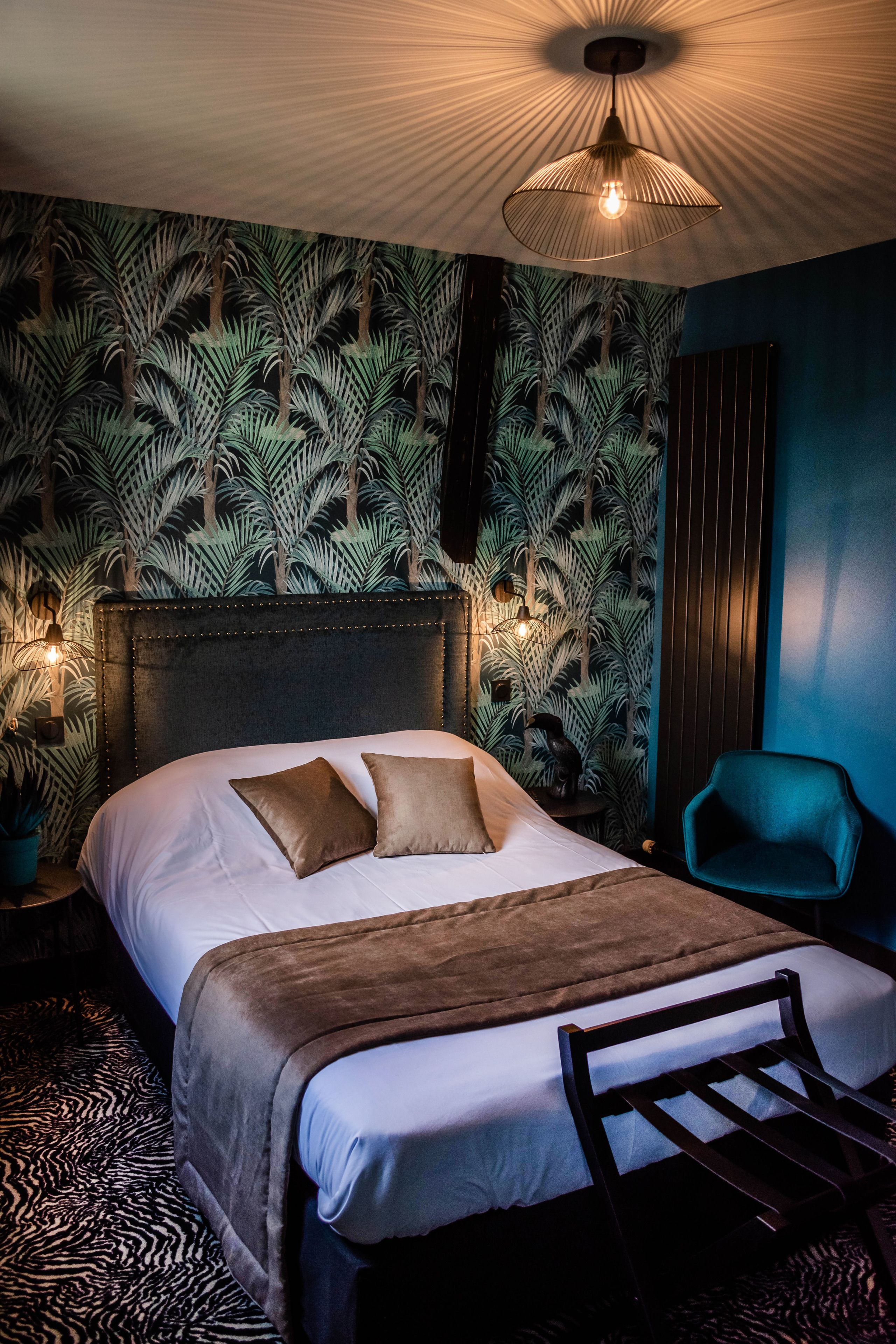 Quarto com cama, cabeceira, luminária na parede, cadeira e carpete estampado.