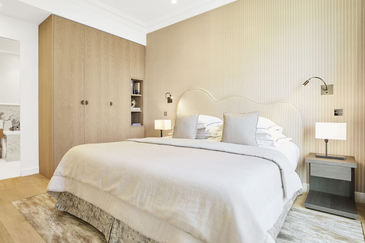 Quarto moderno com uma cama grande, um guarda-roupa de madeira, uma mesa de cabeceira e um criado-mudo.