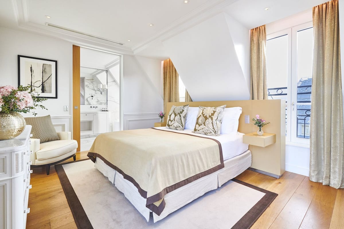 Quarto espaçoso com uma cama grande, mesa de cabeceira, uma cadeira e vista para a cidade pela janela.
