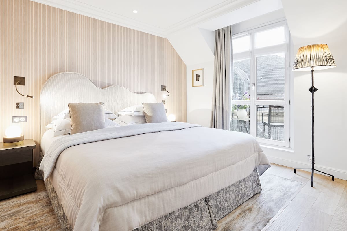 Quarto moderno com uma cama grande, luminárias de cabeceira, mesa de cabeceira, luminária de chão e janela com cortinas.