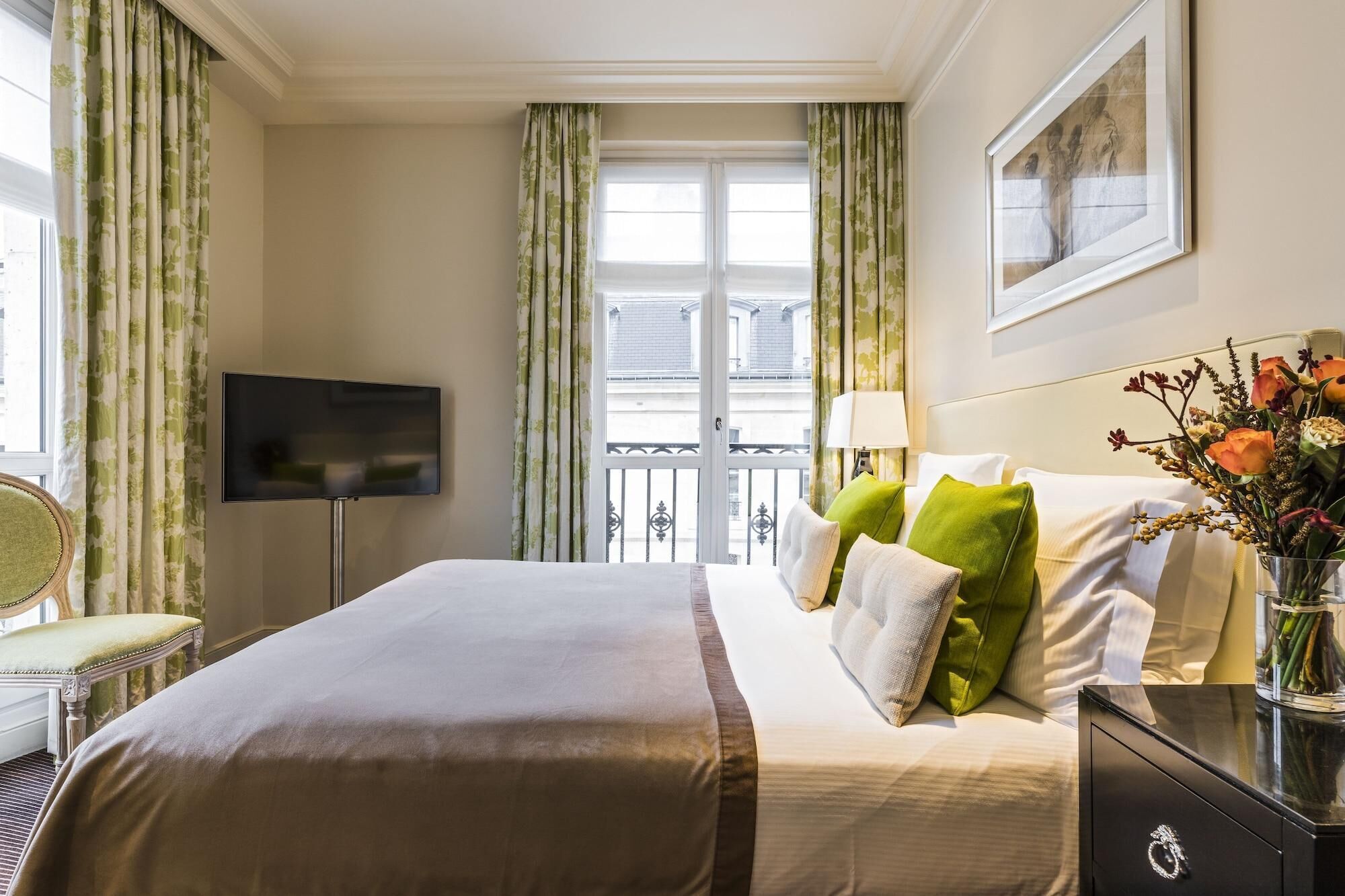 Quarto de hotel com cama, televisão, vista para a varanda e uma obra de arte emoldurada na parede.
