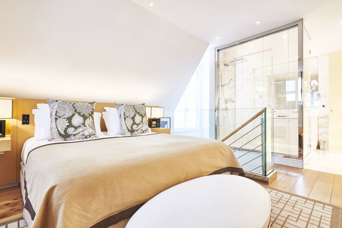 Quarto de hotel moderno com uma cama grande, porta de vidro que dá para uma varanda e uma pequena mesa de cabeceira com uma luminária.