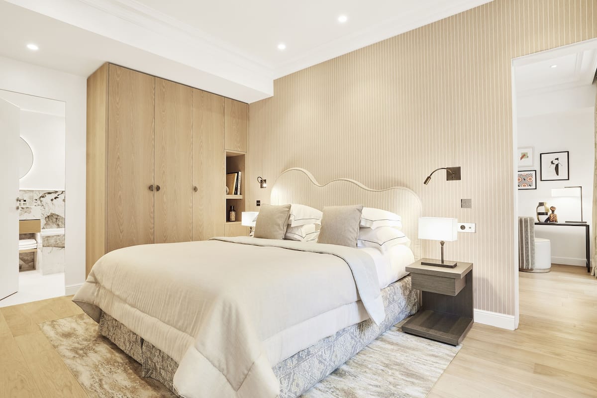 Quarto moderno com cama grande, guarda-roupa de madeira e mesa de cabeceira com abajur.
