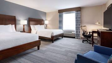 Quarto de hotel com duas camas, uma escrivaninha, uma cadeira e uma televisão.
