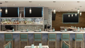 Uma área de bar moderna com um balcão extenso, banquetas e diversas garrafas e copos.