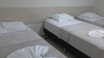 Quarto de hotel com duas camas de solteiro, cada uma com um edredom branco e travesseiro, e uma toalha branca dobrada no chão.