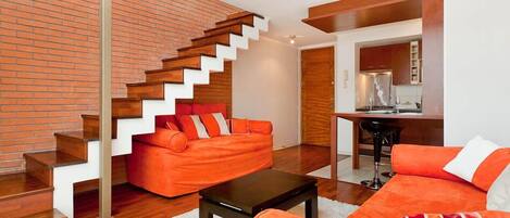 Uma sala de estar moderna com escada de madeira, sofá laranja e área de cozinha.