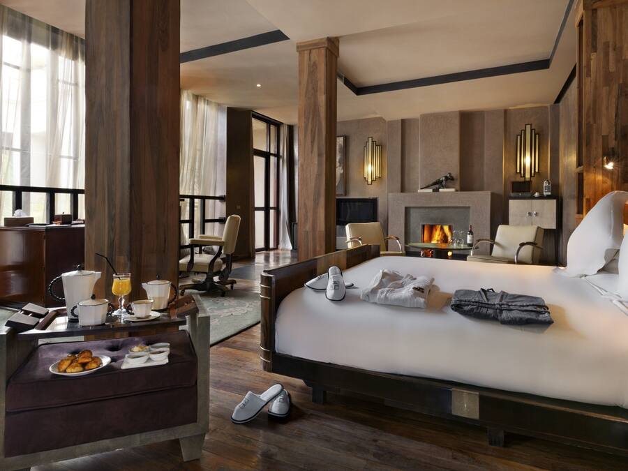 Quarto de hotel moderno com uma cama grande, uma escrivaninha com itens de café da manhã, lareira e vista para o exterior.