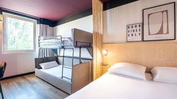 Quarto com beliches, uma cama grande, janela com vista para árvores e parede com obras de arte emolduradas.