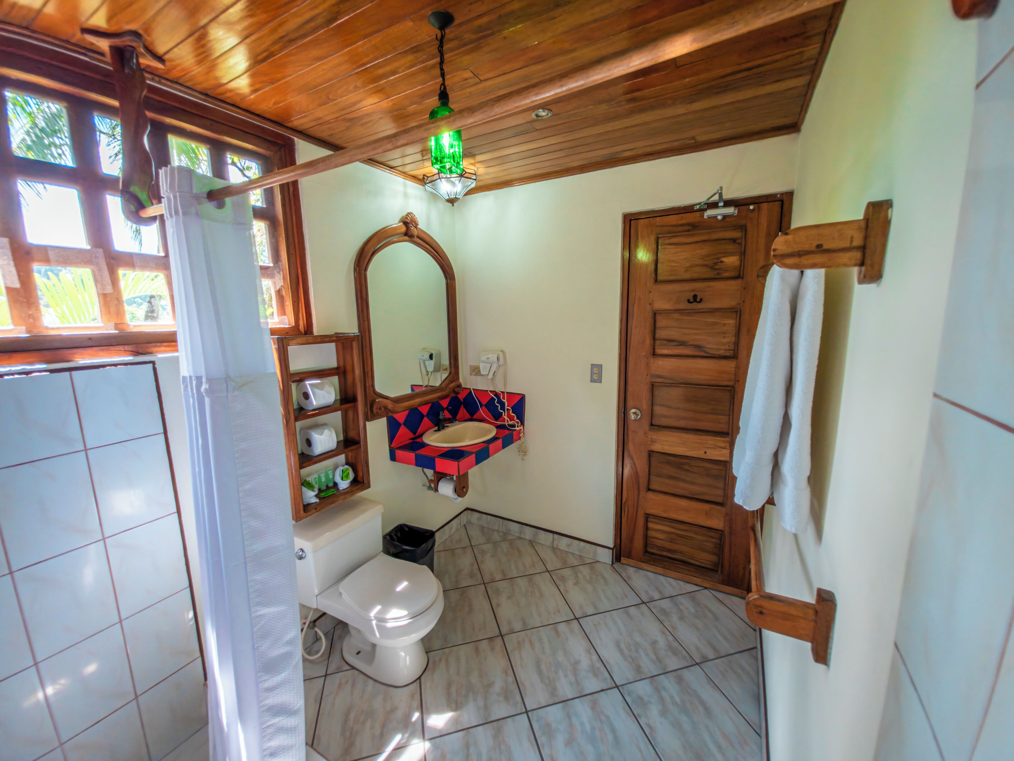 Casa de banho com sanita, lavatório, espelho e porta de madeira.