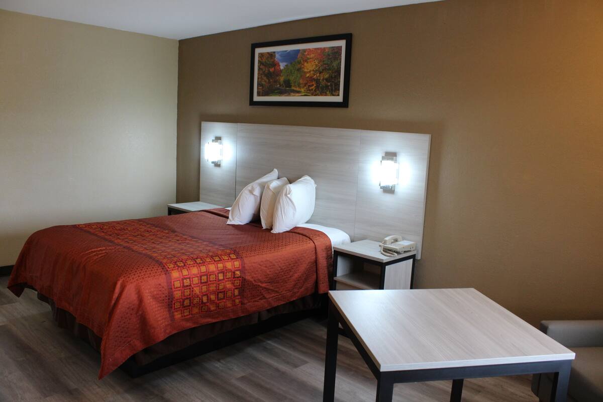 Quarto de hotel com uma cama, mesas de cabeceira, escrivaninha e um quadro na parede.