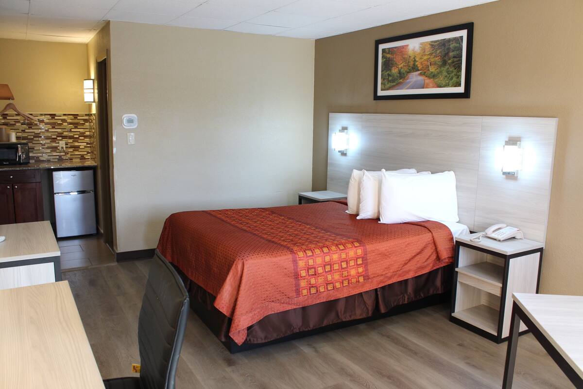 Quarto de hotel com cama, mesas de cabeceira, escrivaninha e cozinha compacta.