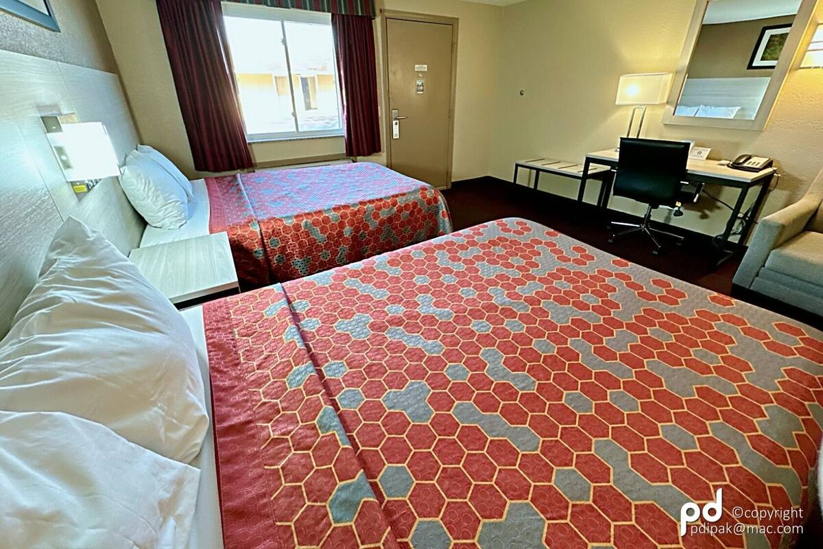 Quarto de hotel com duas camas, uma escrivaninha, uma cadeira e uma janela com cortinas.