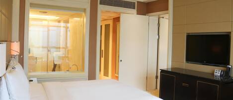 Quarto de hotel com cama, televisão, minibar e banheiro visível por uma porta aberta.