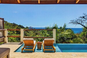 Uma área de piscina ao ar livre com espreguiçadeiras de madeira e vista para o oceano.