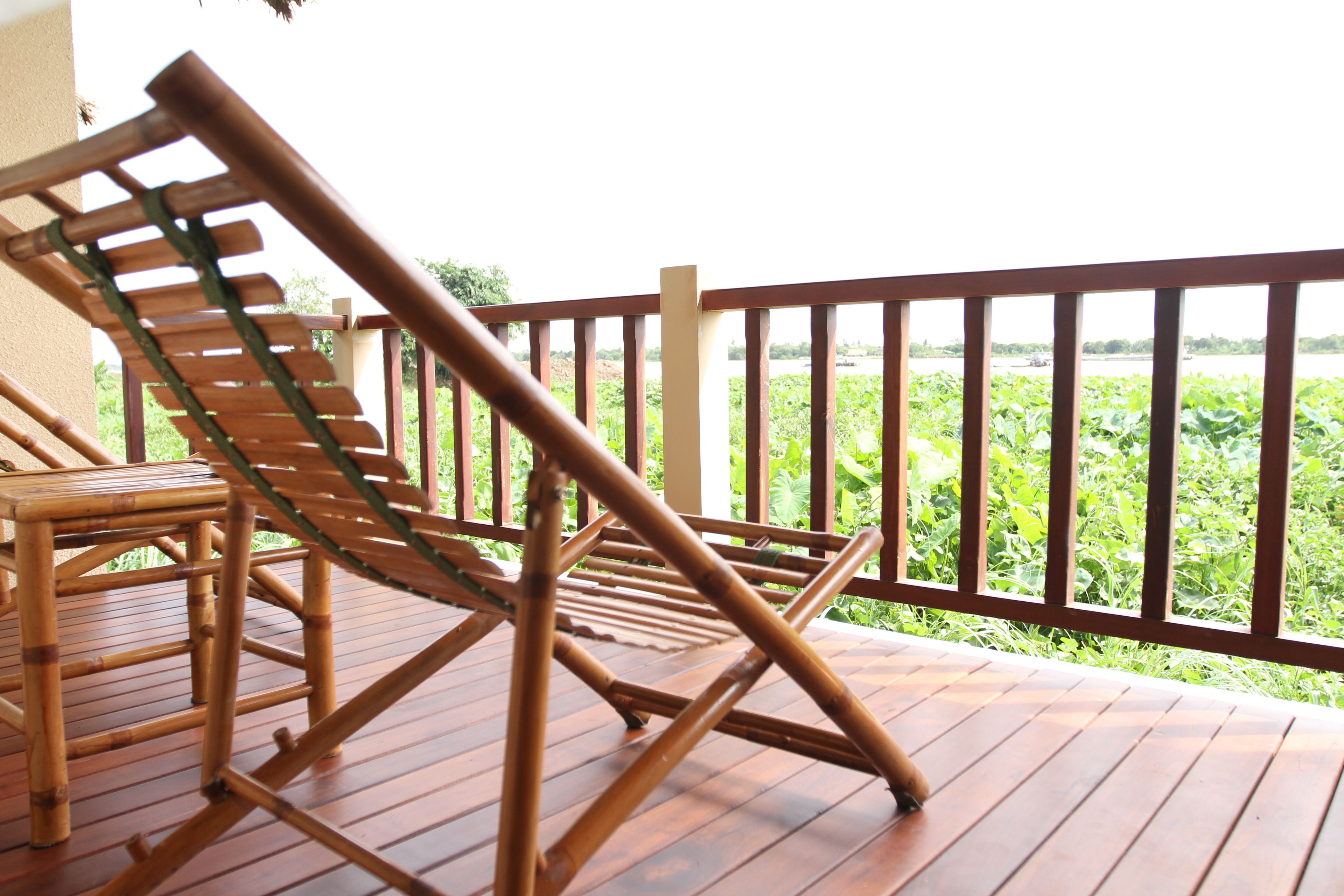 Um deck de madeira com uma cadeira de bambu e uma mesa, com vista para uma paisagem verdejante.