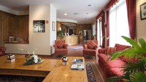 Uma sala de estar espaçosa com uma mesa de centro de madeira, sofás vermelhos estampados e uma mesa de recepção ao fundo.