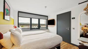 Quarto de hotel moderno com uma cama grande, uma mesa de escritório e uma janela com vista para a cidade.
