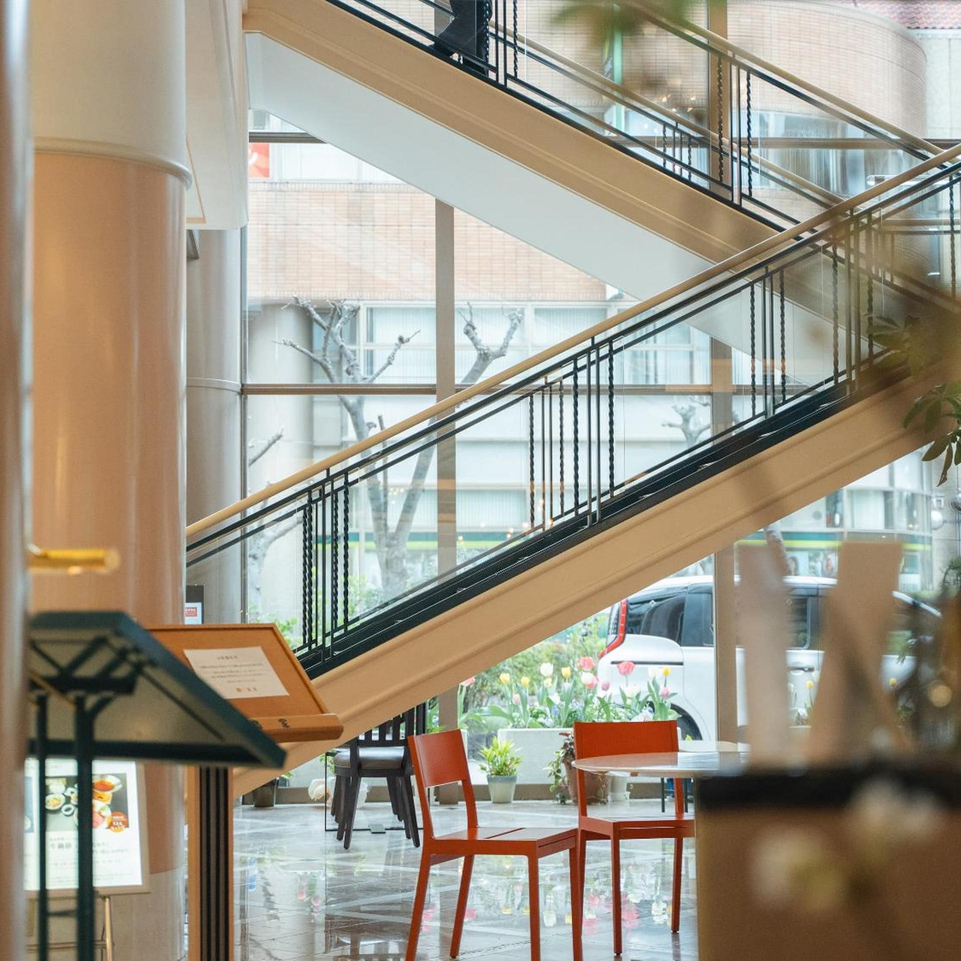 Espaço interno com escada de vidro, mesa com cadeiras e vista para o exterior.
