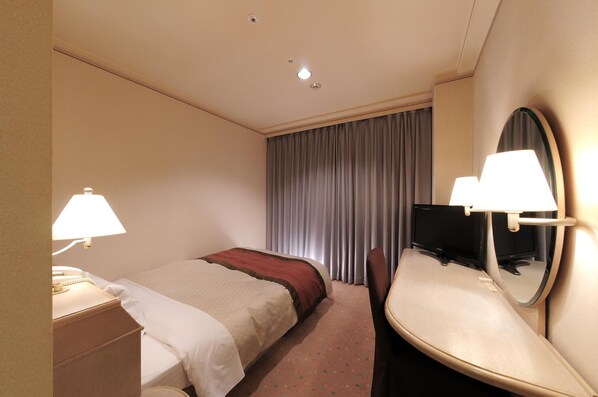 Quarto de hotel com cama, mesa de cabeceira, luminária, espelho e cortinas.