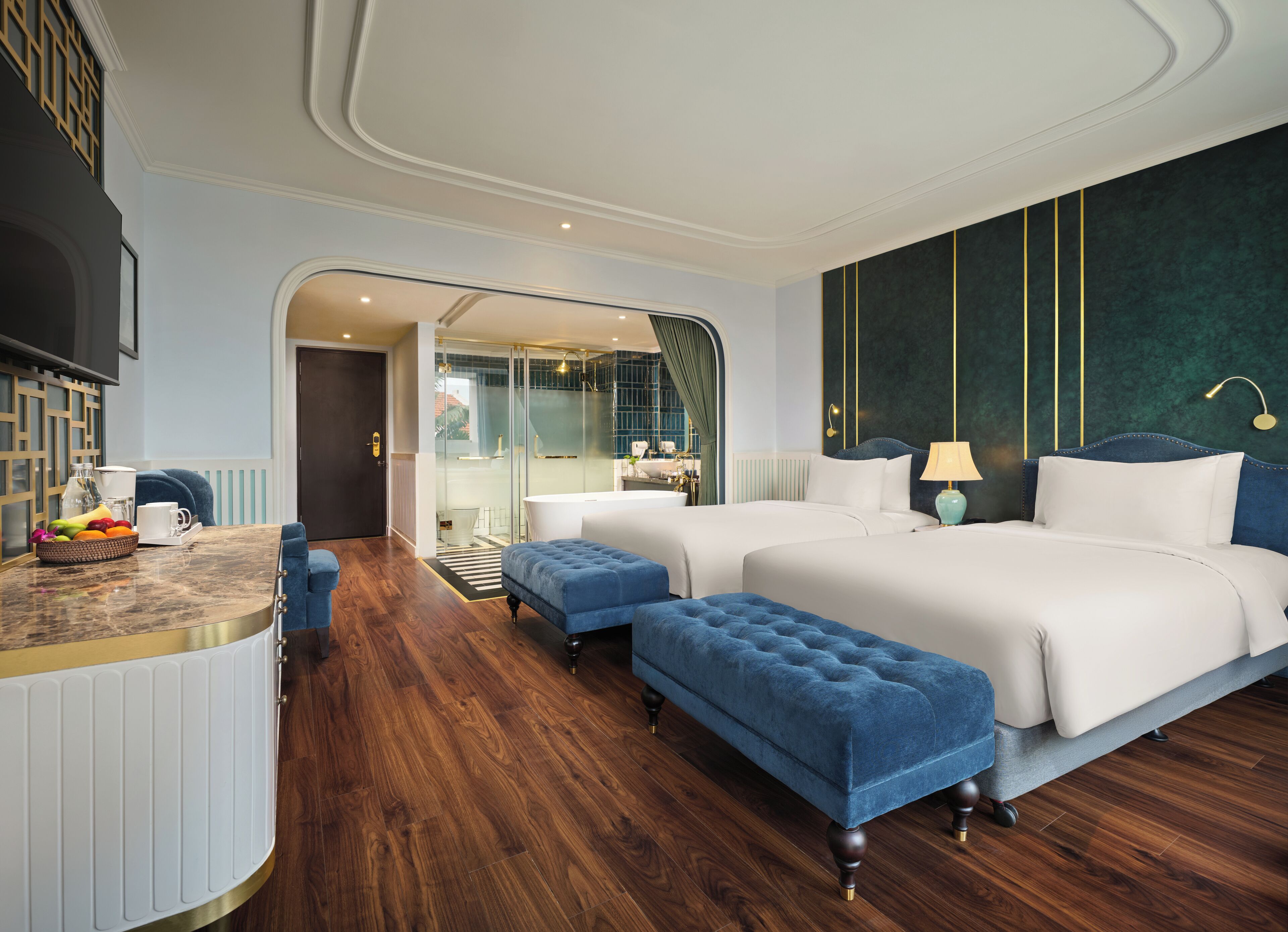 Quarto de hotel moderno com duas camas, um espaço de estar com mesa de centro e vista da cidade através de uma porta de vidro.