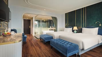 Quarto de hotel moderno com duas camas, um espaço de estar com mesa de centro e vista da cidade através de uma porta de vidro.