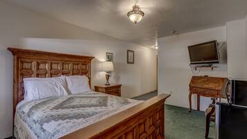 Quarto com cama de madeira, mesa de cabeceira, luminária, cômoda e televisão.