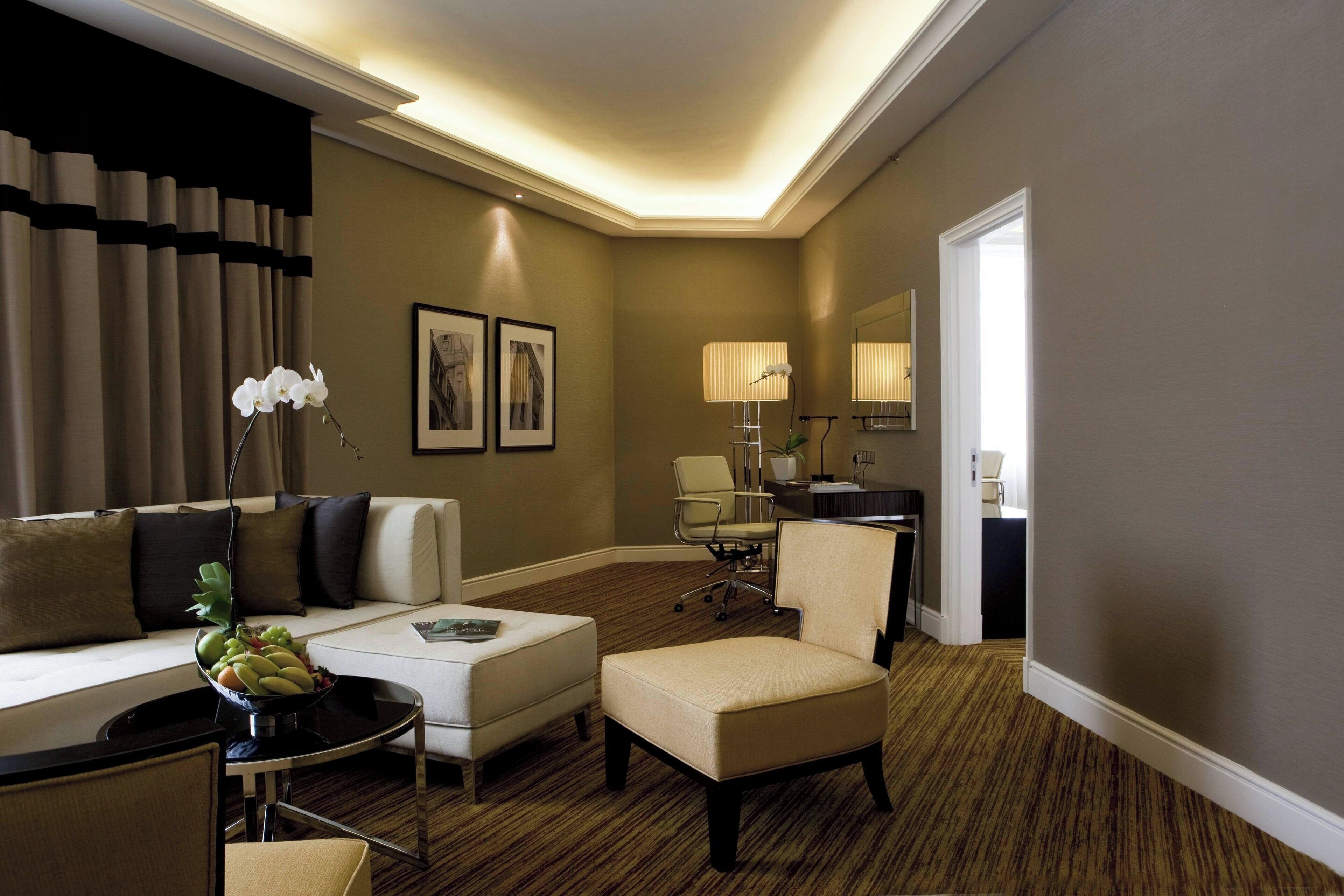 Quarto de hotel com sofá, poltrona, mesa de jantar e pequena escrivaninha com abajur.