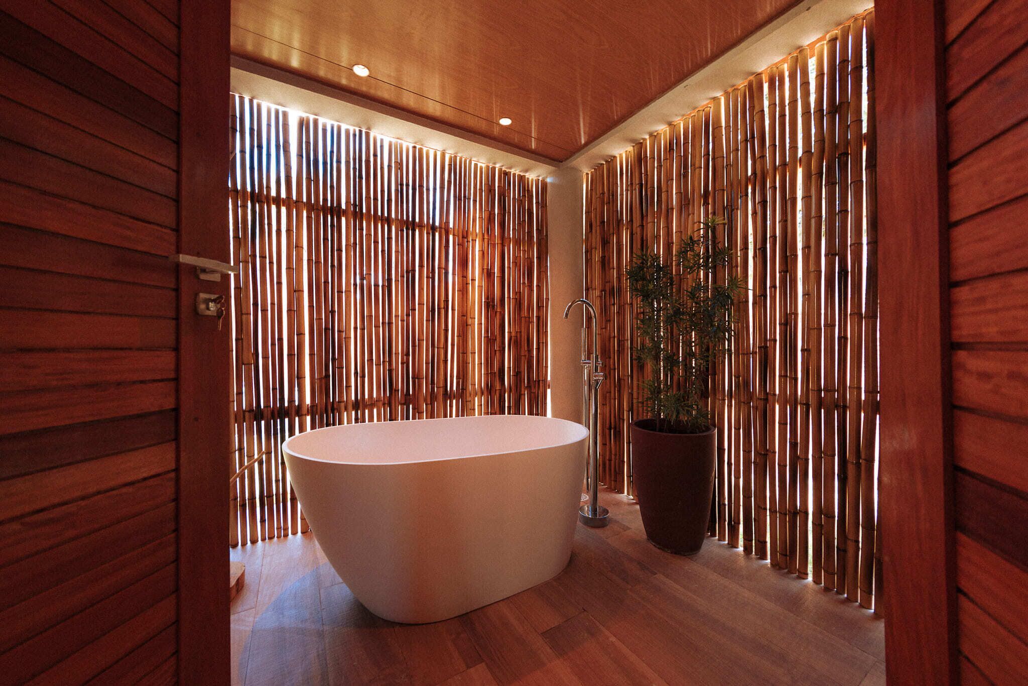 Um banheiro moderno com uma banheira de imersão, painéis de parede de bambu e um vaso de planta.