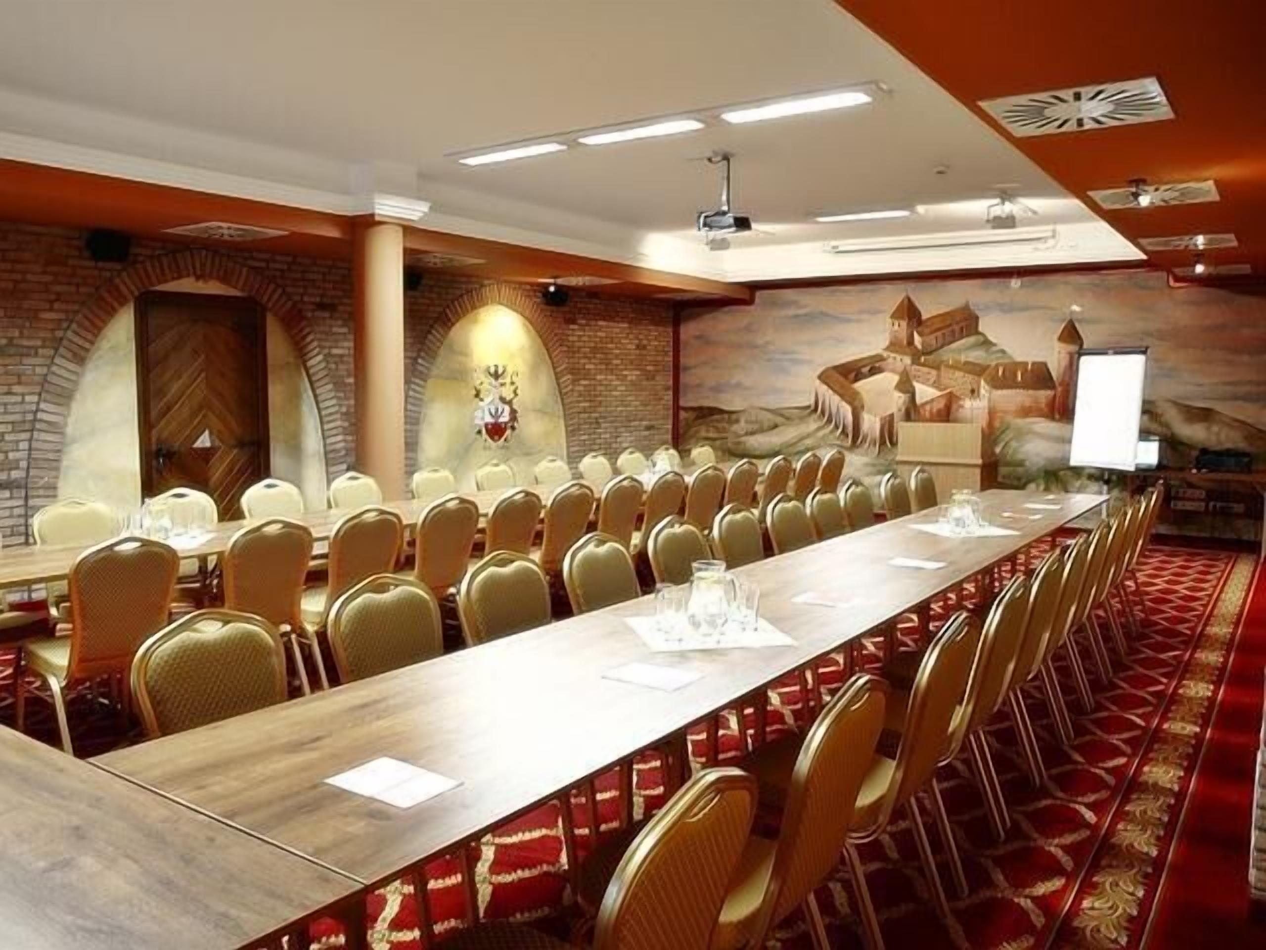 Uma sala de conferências com uma mesa comprida, várias cadeiras, uma tela de projetor e um mural decorativo na parede.