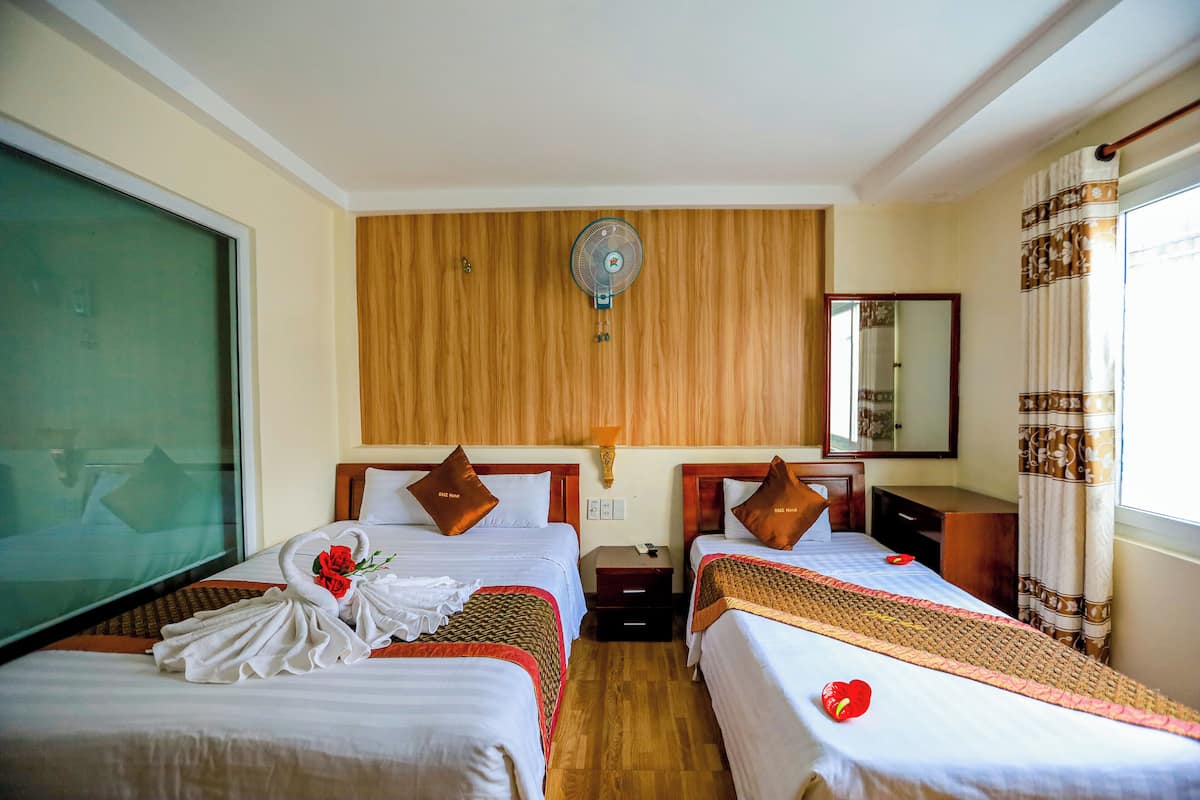 Quarto de hotel com duas camas, cabeceira de madeira, ventoinha na parede, espelho e janela com cortinas.