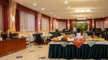 Uma sala de banquetes com mesas redondas, um buffet e um espaço para café.