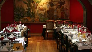 Restaurante com mesas preparadas para refeições, um mural na parede e piso de madeira.